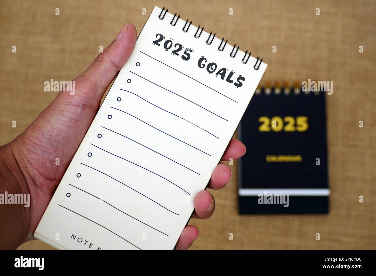 Hand-holding a checklist book for 2025 goals with 2025 calendar. New ...