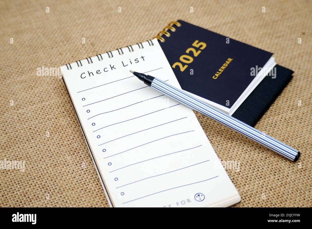 A blank checklist notebook sits next to a small 2025 calendar on a ...