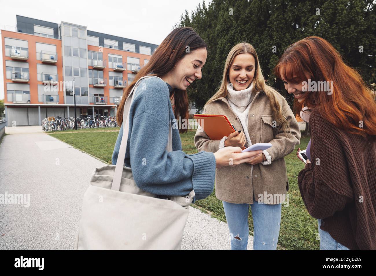 Group of three cheerful female collage students outside their dorm on a ...