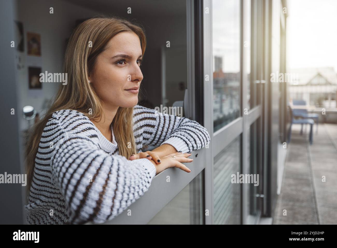 Young blonde caucasian woman looking out the window of her dorm room ...