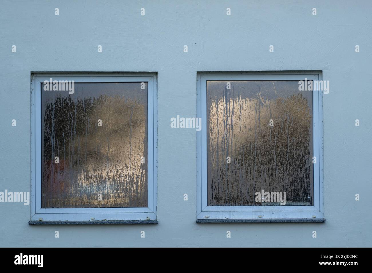 Condensation forming on two windows of a building with a pale blue wall ...