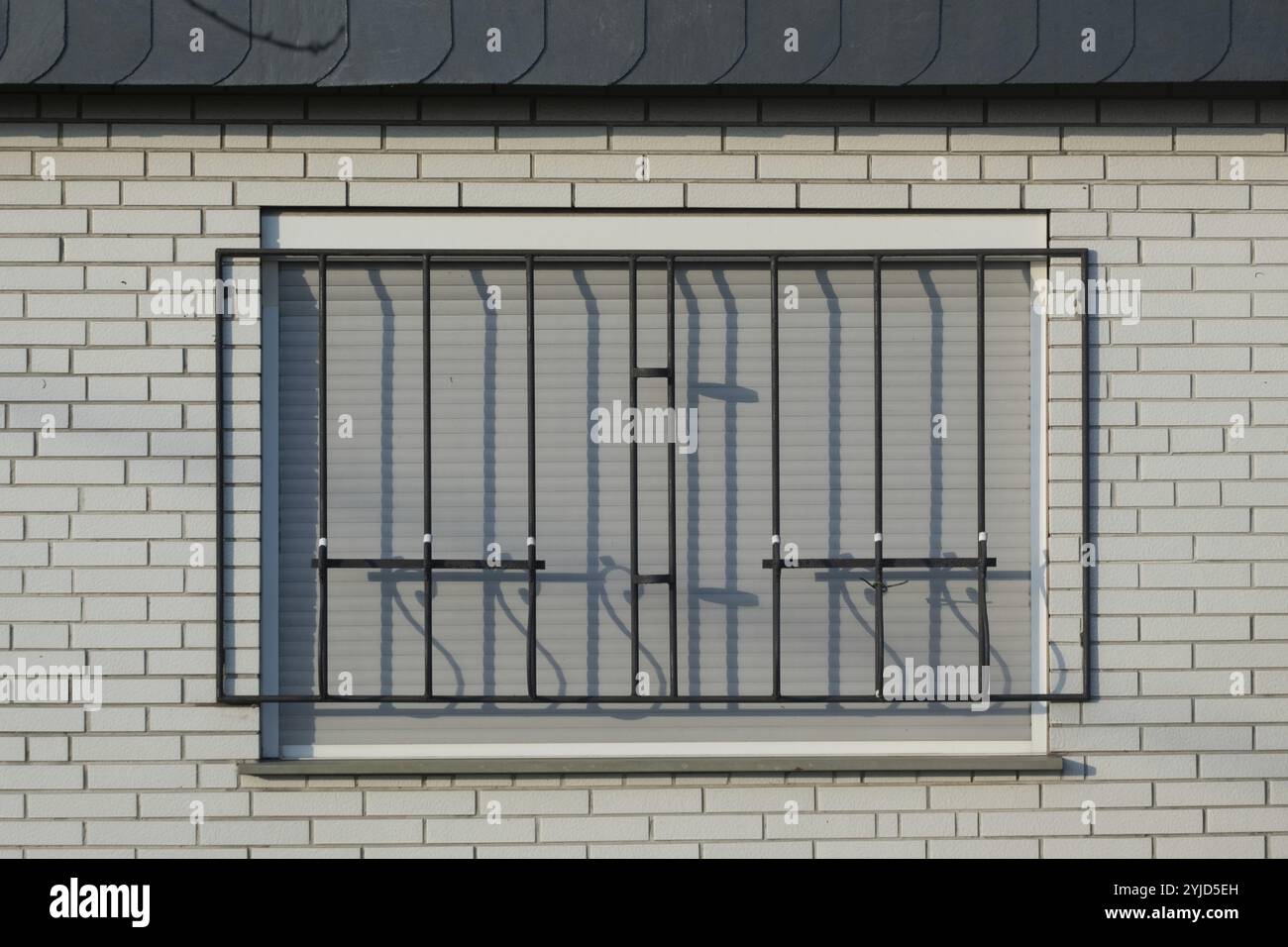 Metal bars covering window on white brick wall with lowered blinds ...