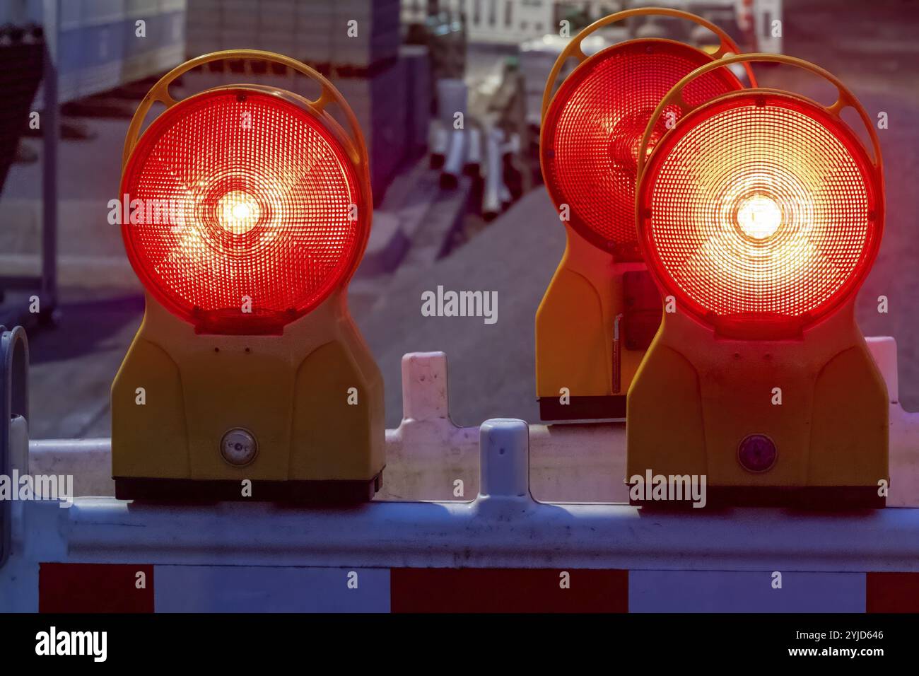 Red warning lights are flashing on a construction site barrier at dusk ...