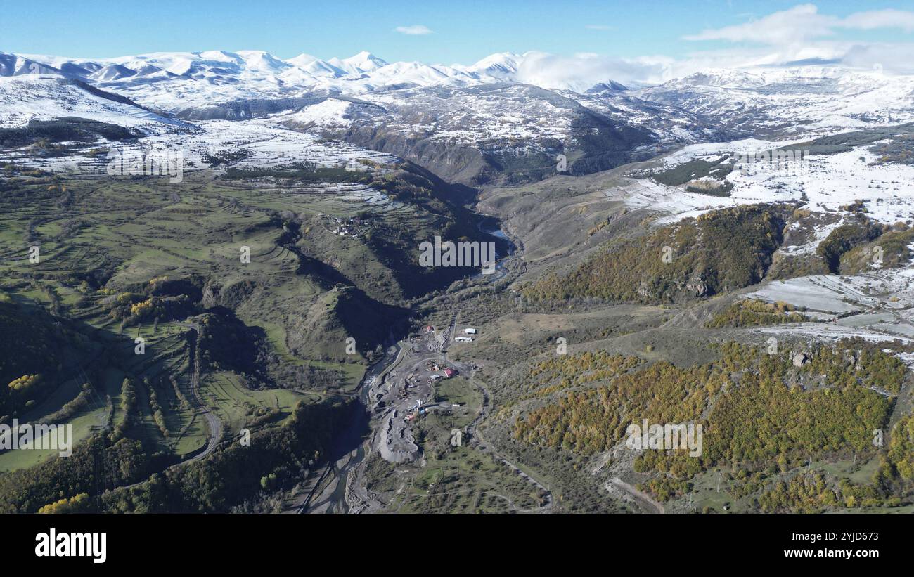 Aerial view of snowy mountains and green valleys under a clear blue sky ...