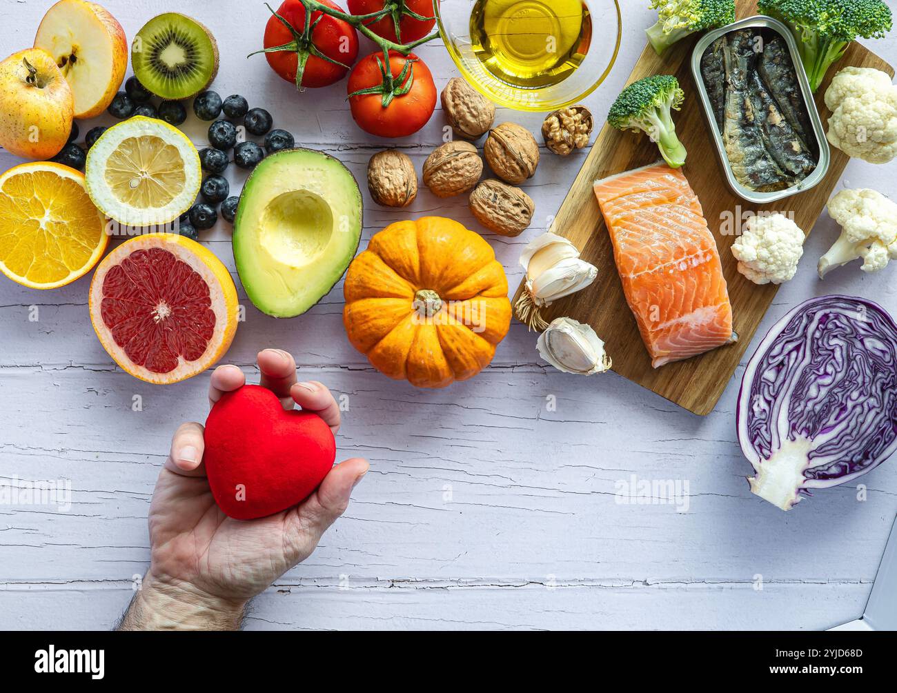 One hand clutches a red heart surrounded by healthy foods to prevent ...
