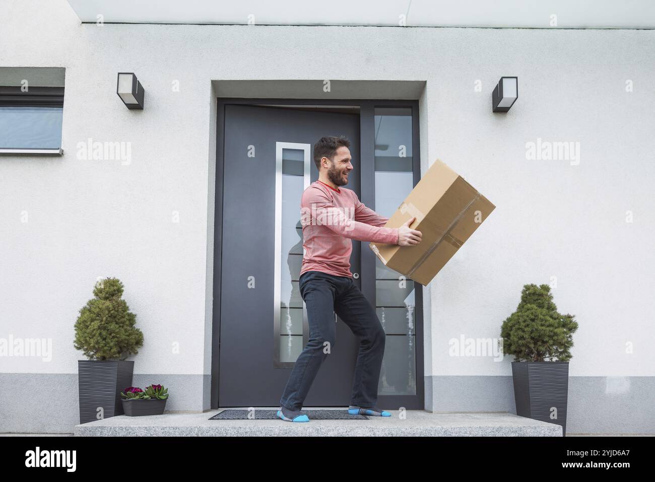 Thrilled caucasian man standing at the front door with a big cardboard ...