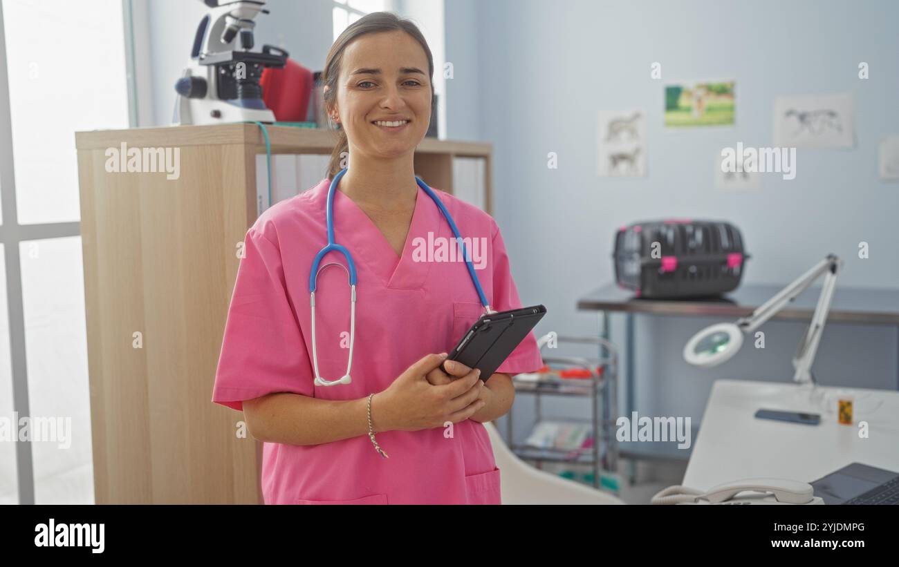 A female nurse in pink scrubs with a stethoscope and tablet smiles in a ...