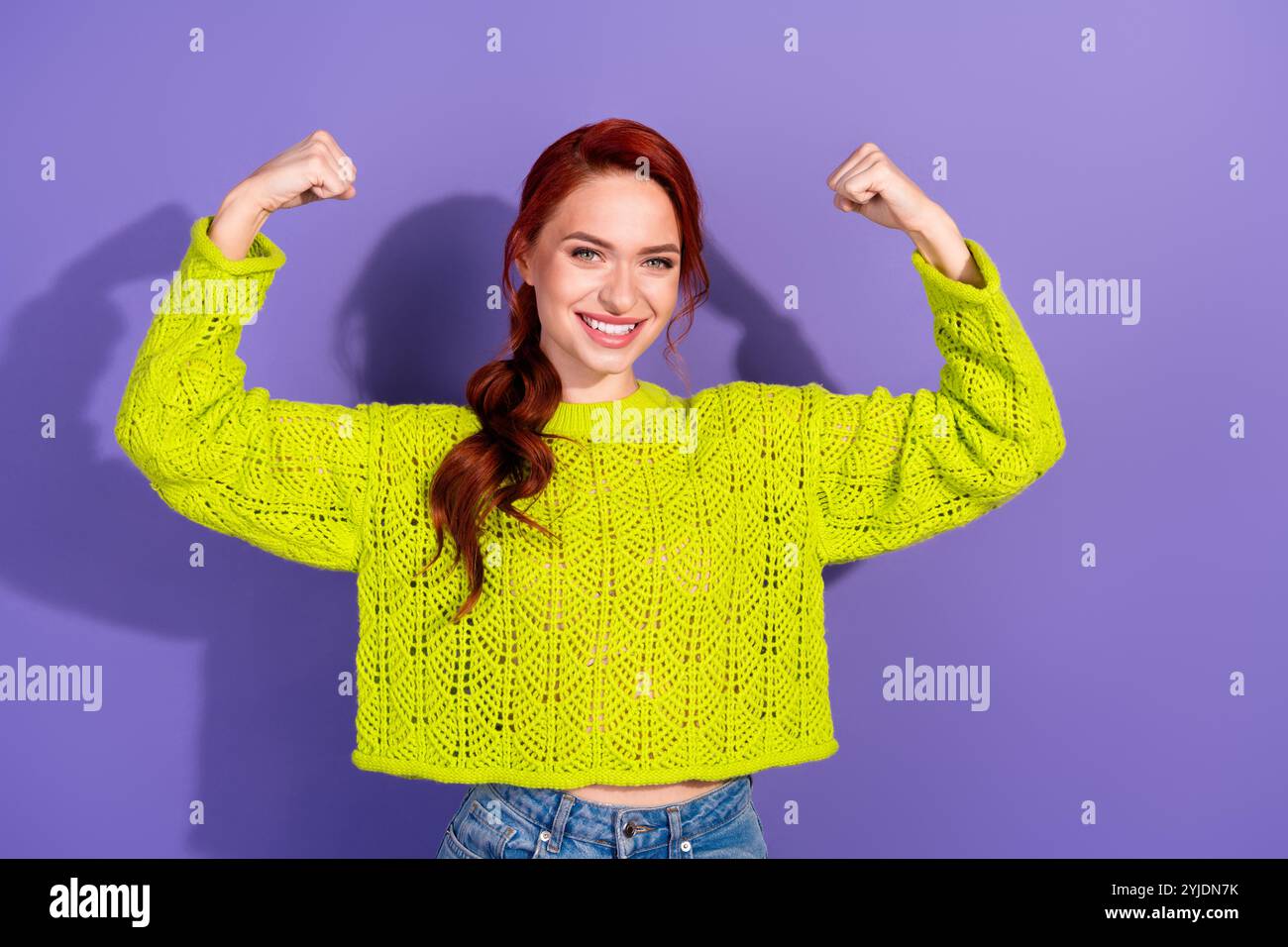 Confident young red-haired woman in green sweater showing strength ...