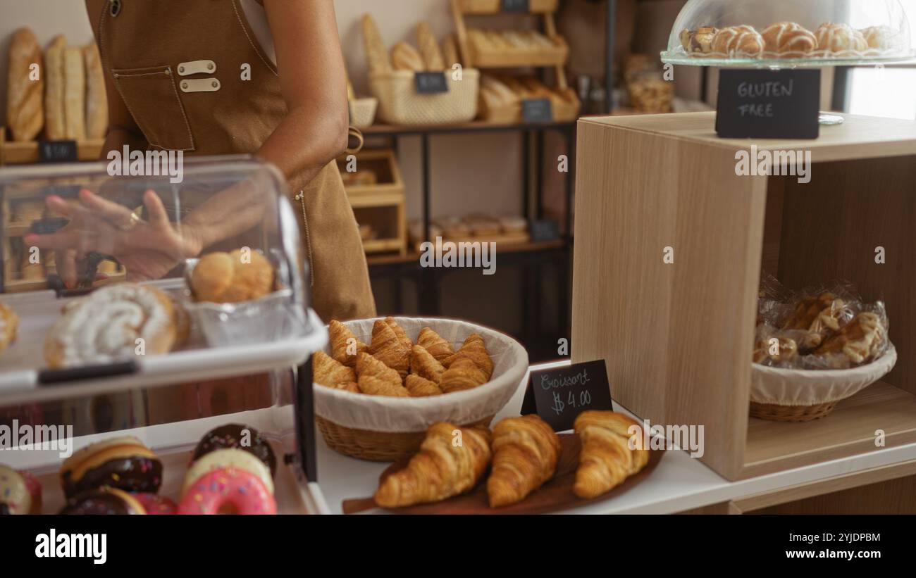 Young hispanic woman arranging pastries in a bakery with hands visible ...
