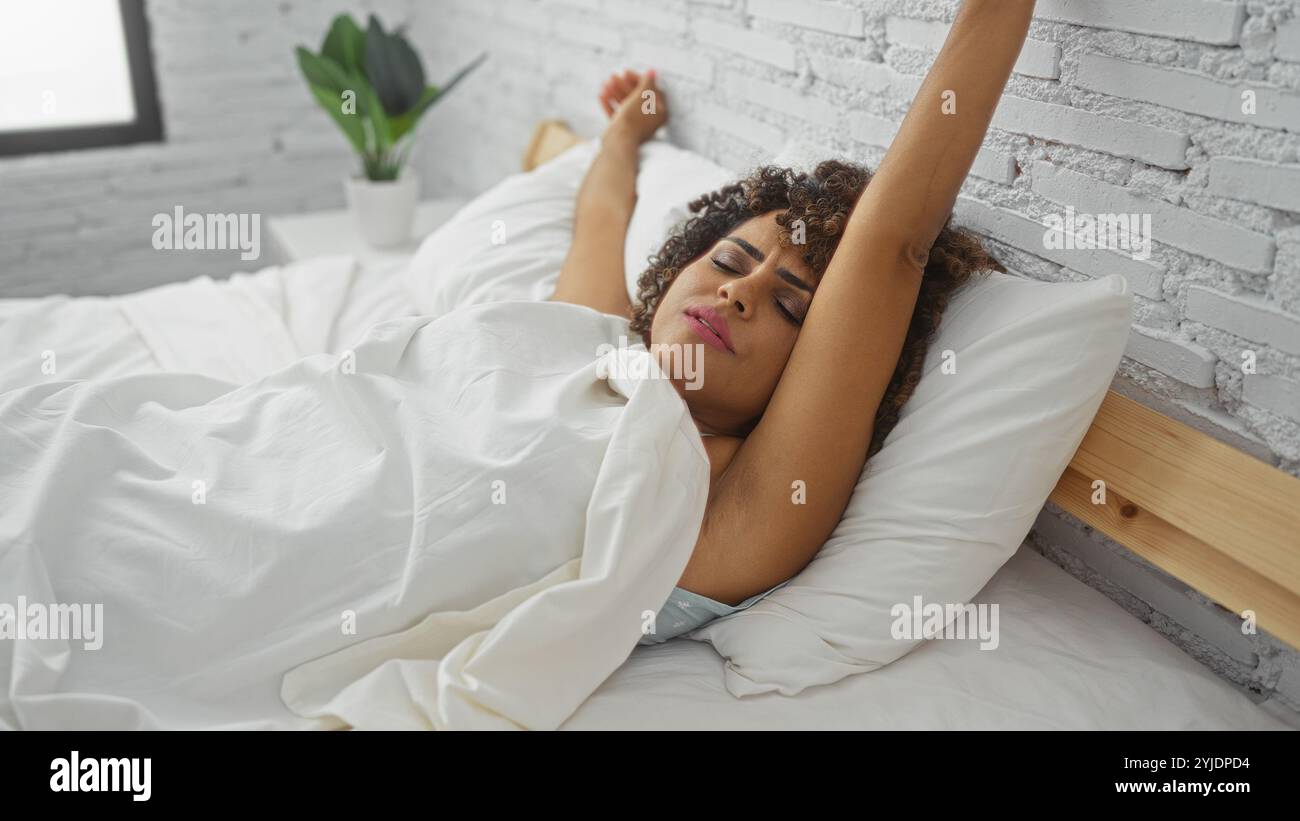 Woman waking up in bed with white sheets in a bright bedroom with white ...