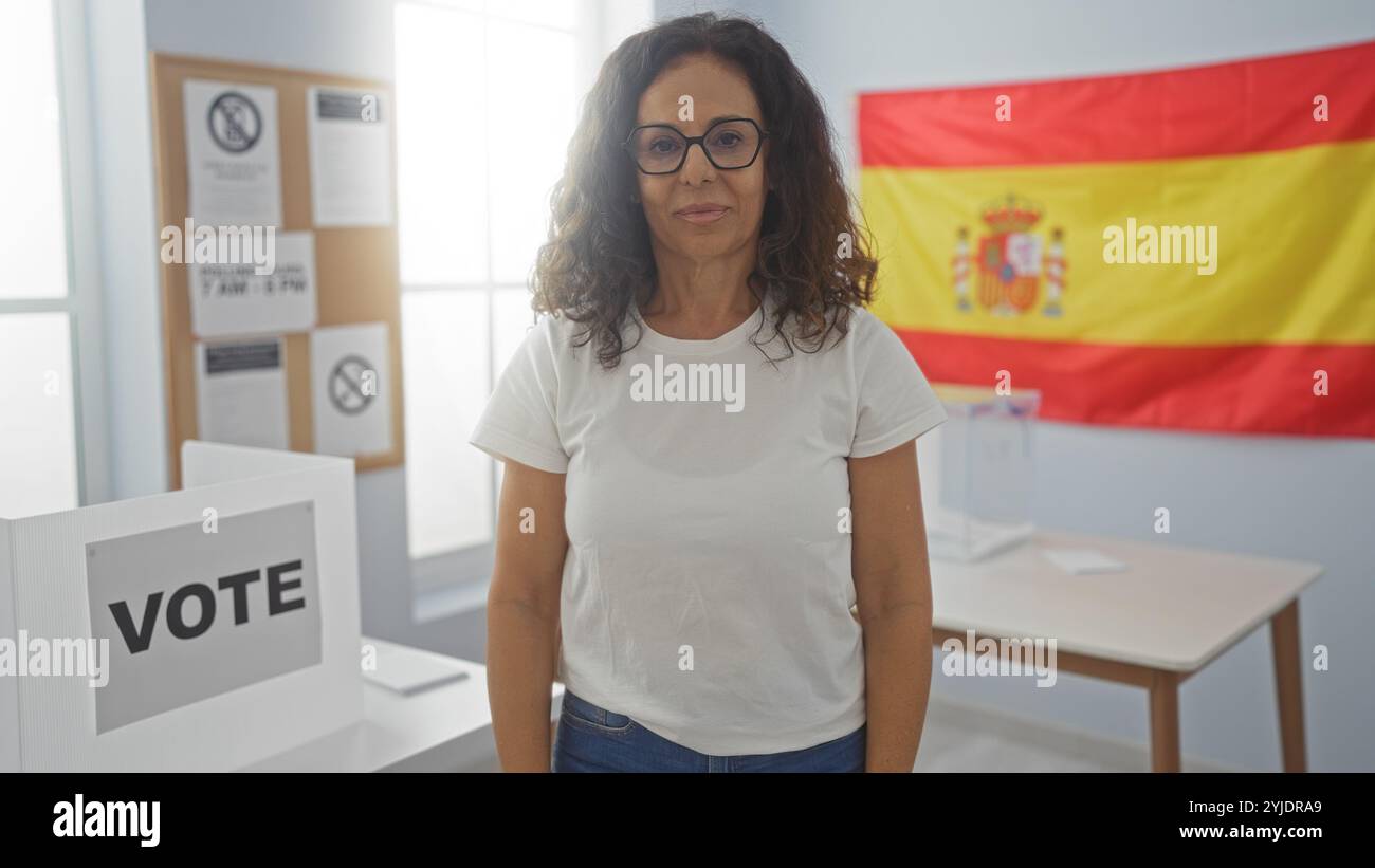 Woman standing indoors at a voting room with a spanish flag, indicating ...