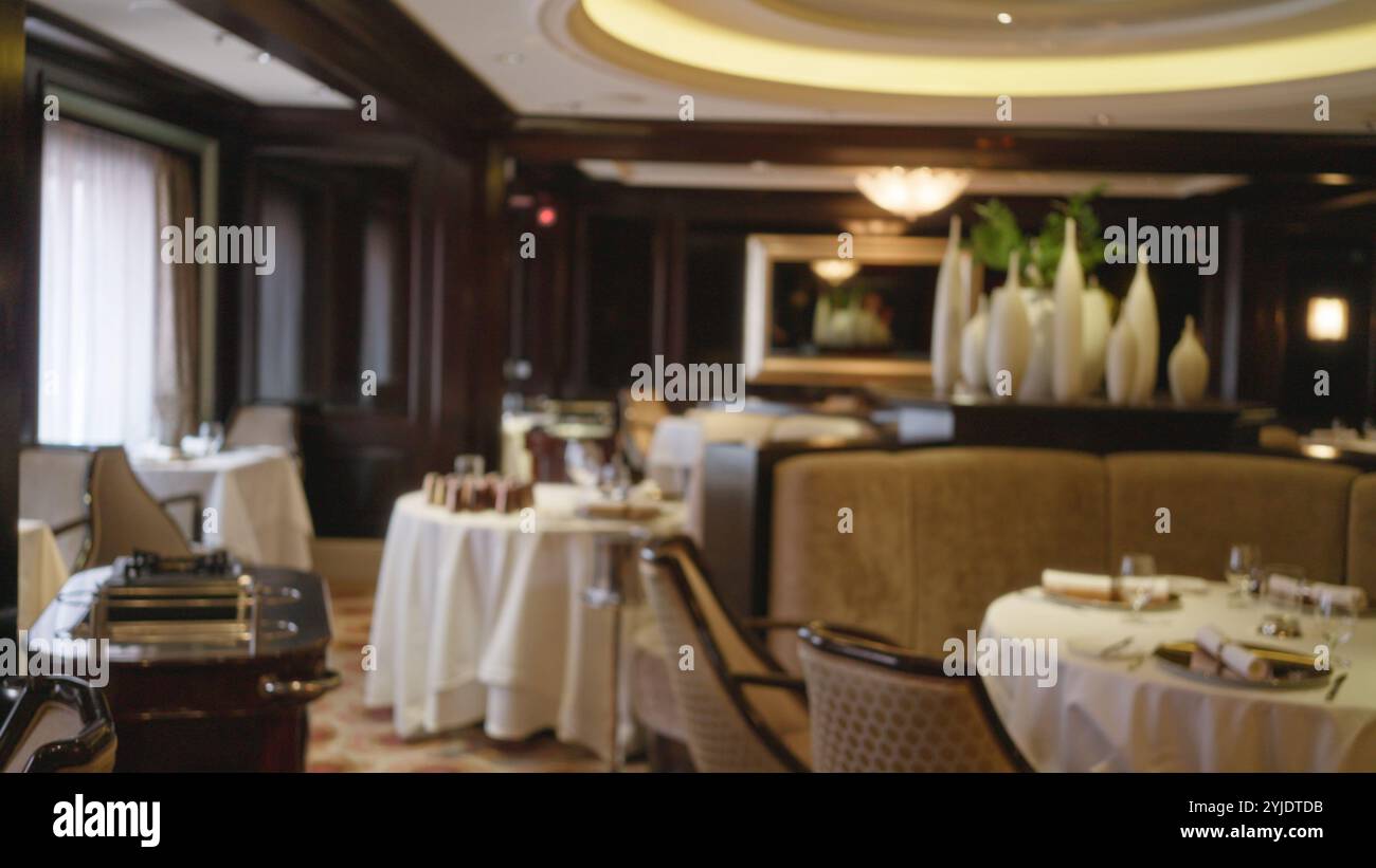 Blurred luxurious restaurant interior with elegant table settings, dim ...