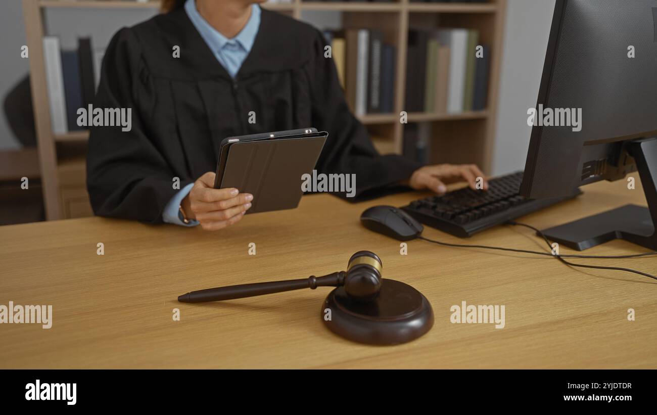 Female judge working on a tablet and computer in an office with a gavel ...