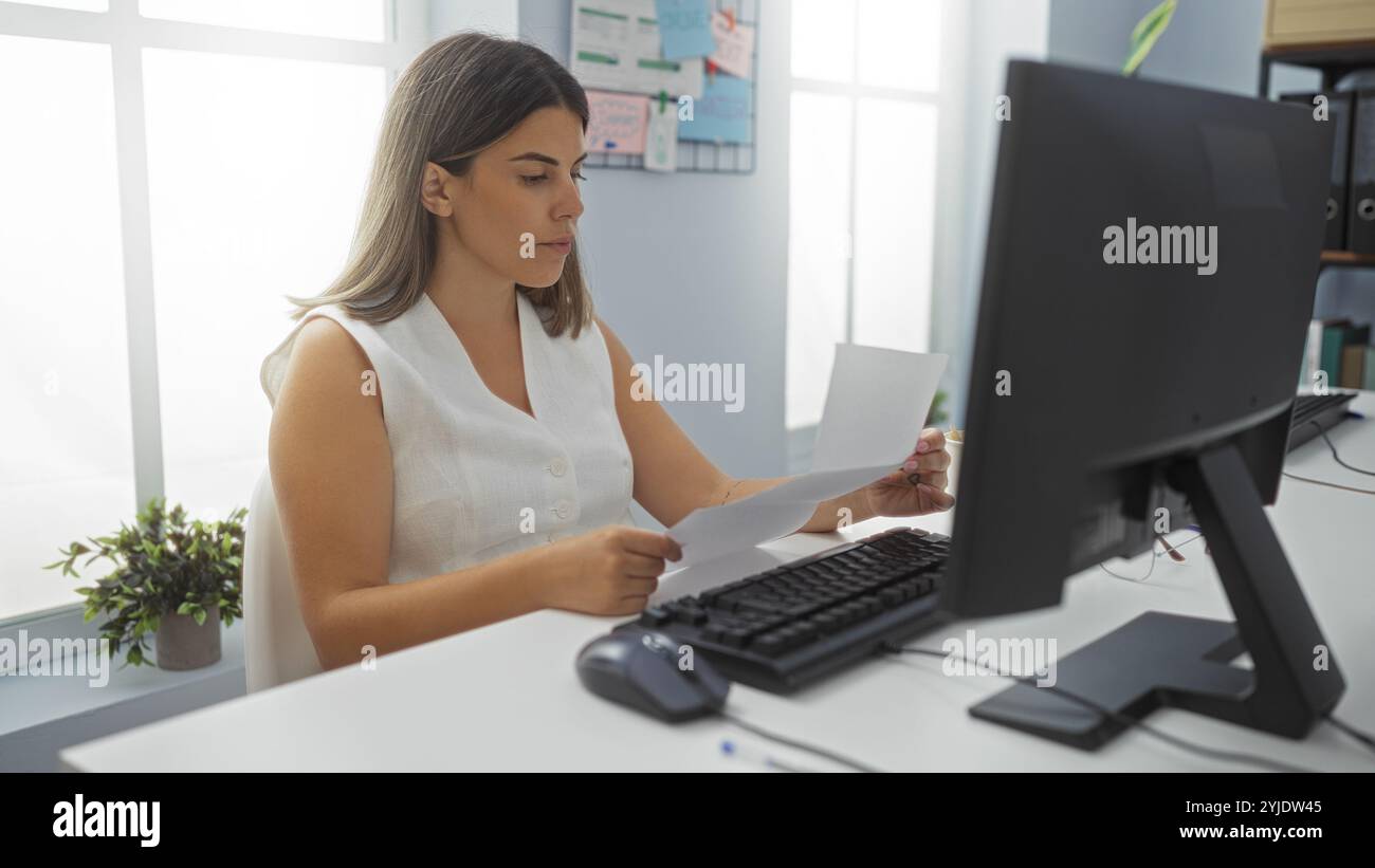 Woman reviewing documents at office desk with computer and plant ...