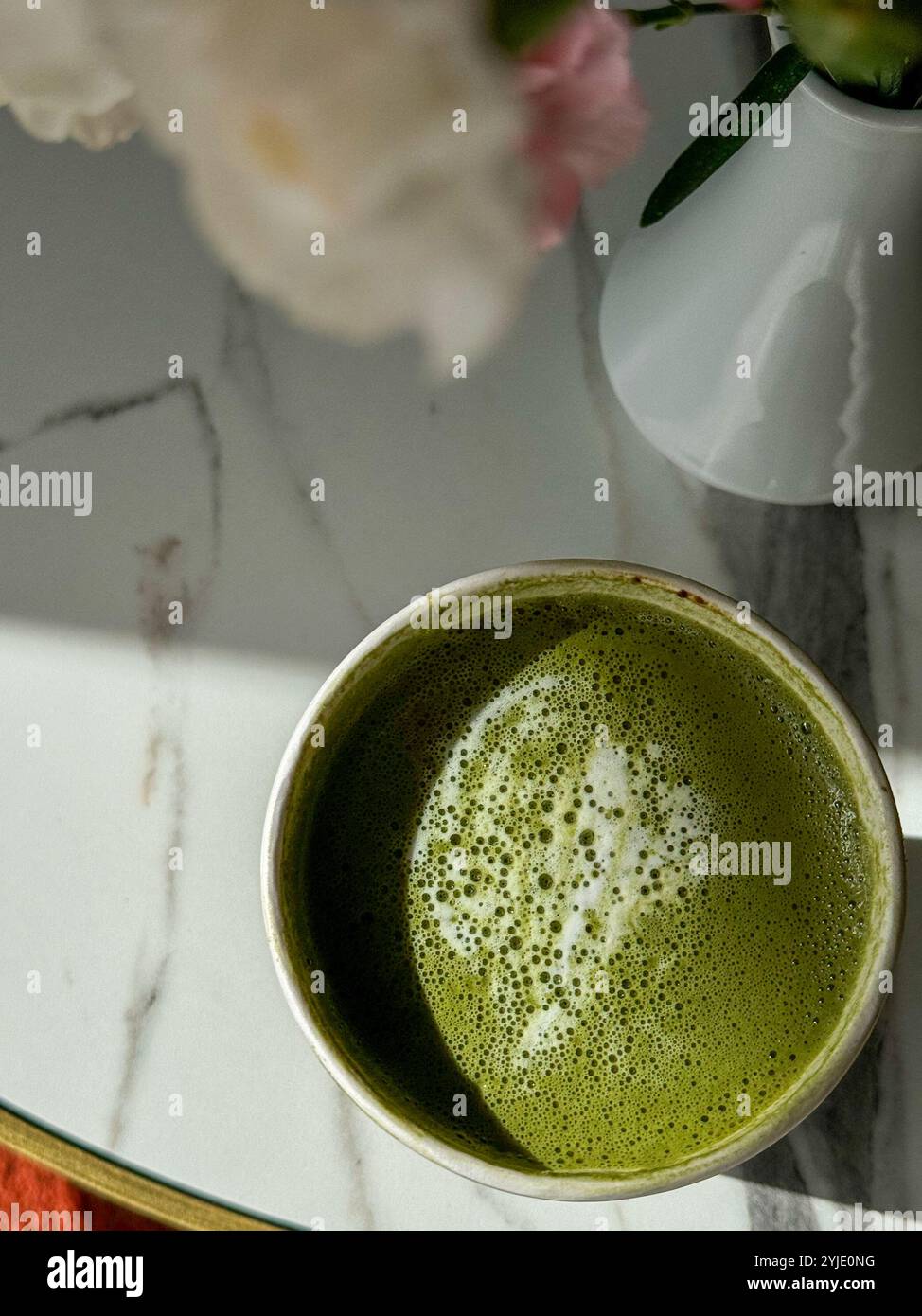 A beautifully crafted cup of matcha tea alongside fresh pink flowers on ...