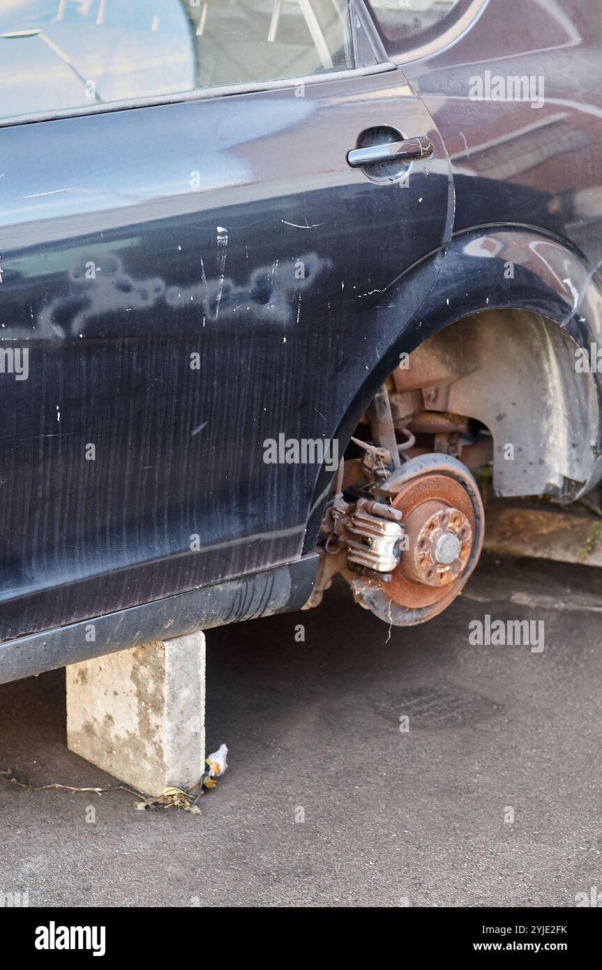 The image captures a car with a stolen wheel, resting on a block for ...