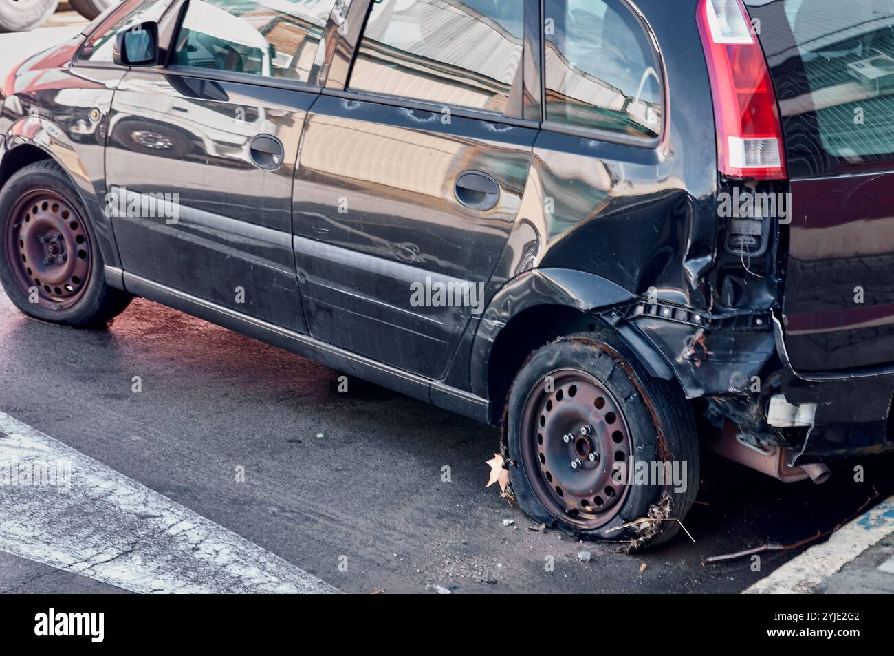 This image shows a black car with significant damage to its rear left ...