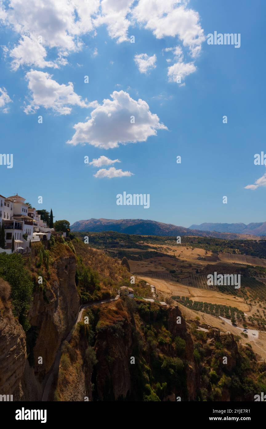 Ronda’s dramatic cliffs and sunlit countryside under a bright blue sky ...