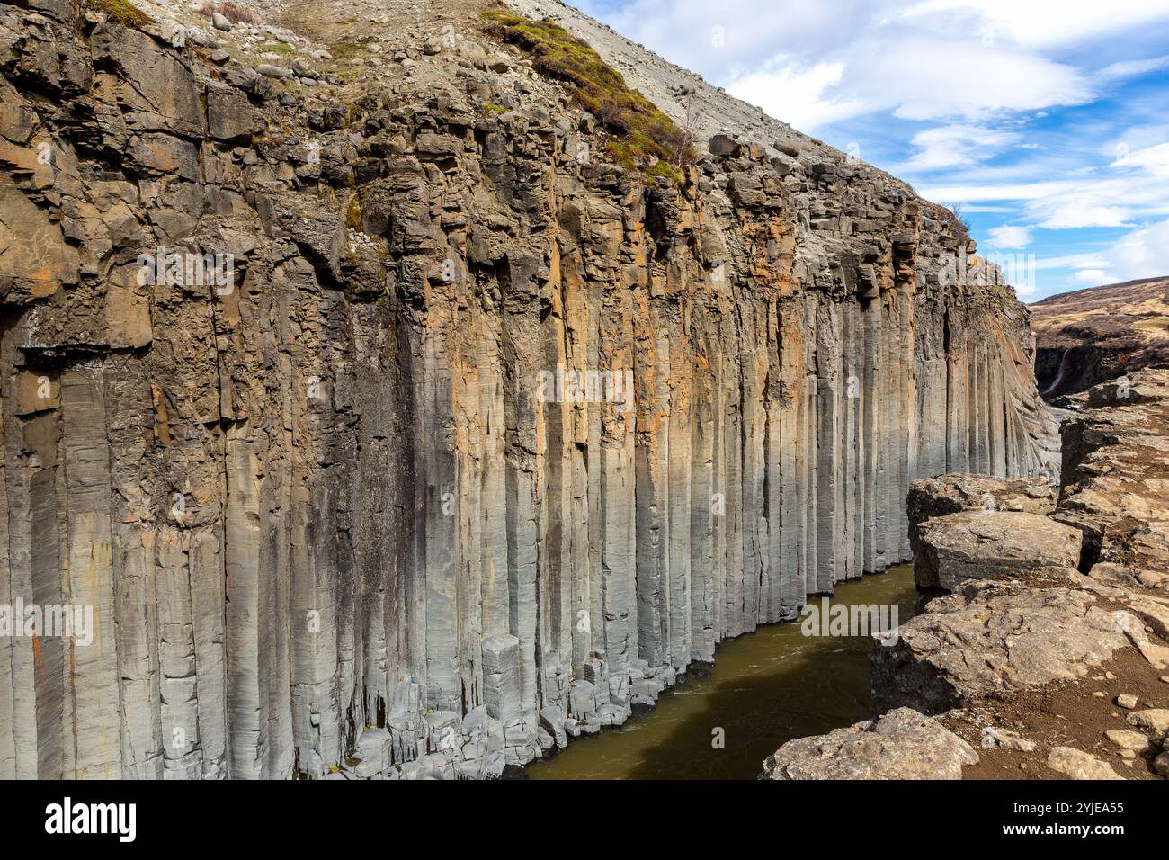 Studlagil Canyon (The Basalt Canyon) view of the ravine with brown glacial river and vertical ...