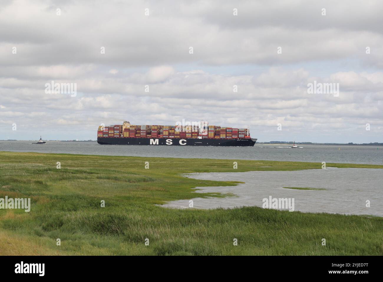 a big container ship is navigating with two tugs through the ...