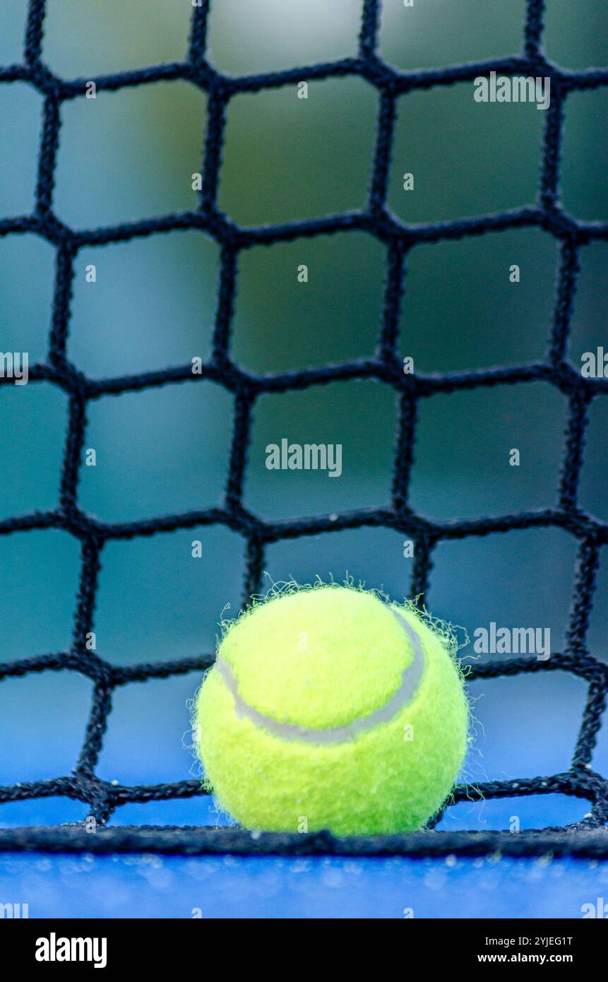 a ball at the base of the net of a paddle court with the background out ...