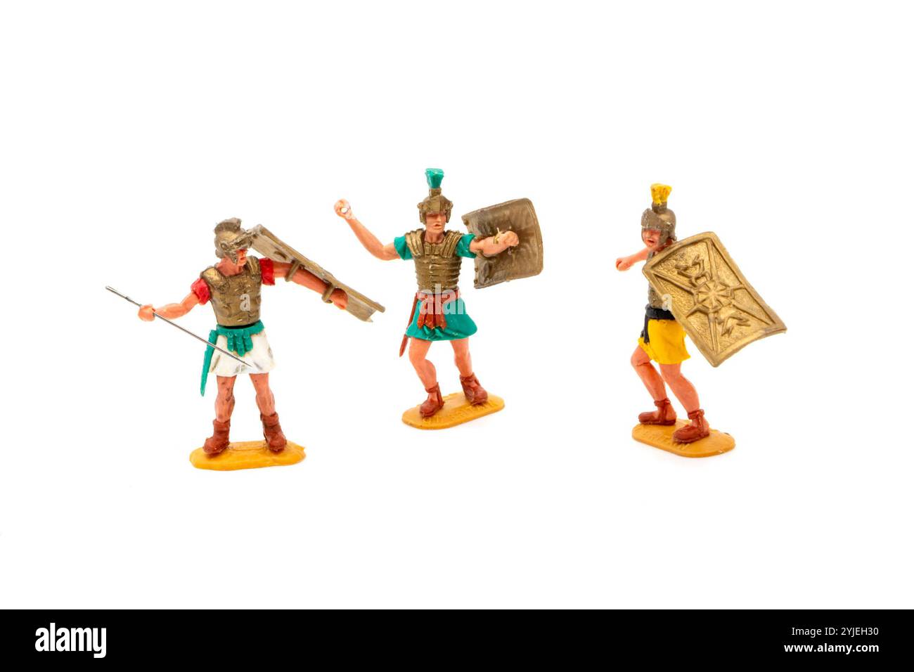 Three toy Roman soldiers in combat poses with helmets, spears, and shields on a white background ...