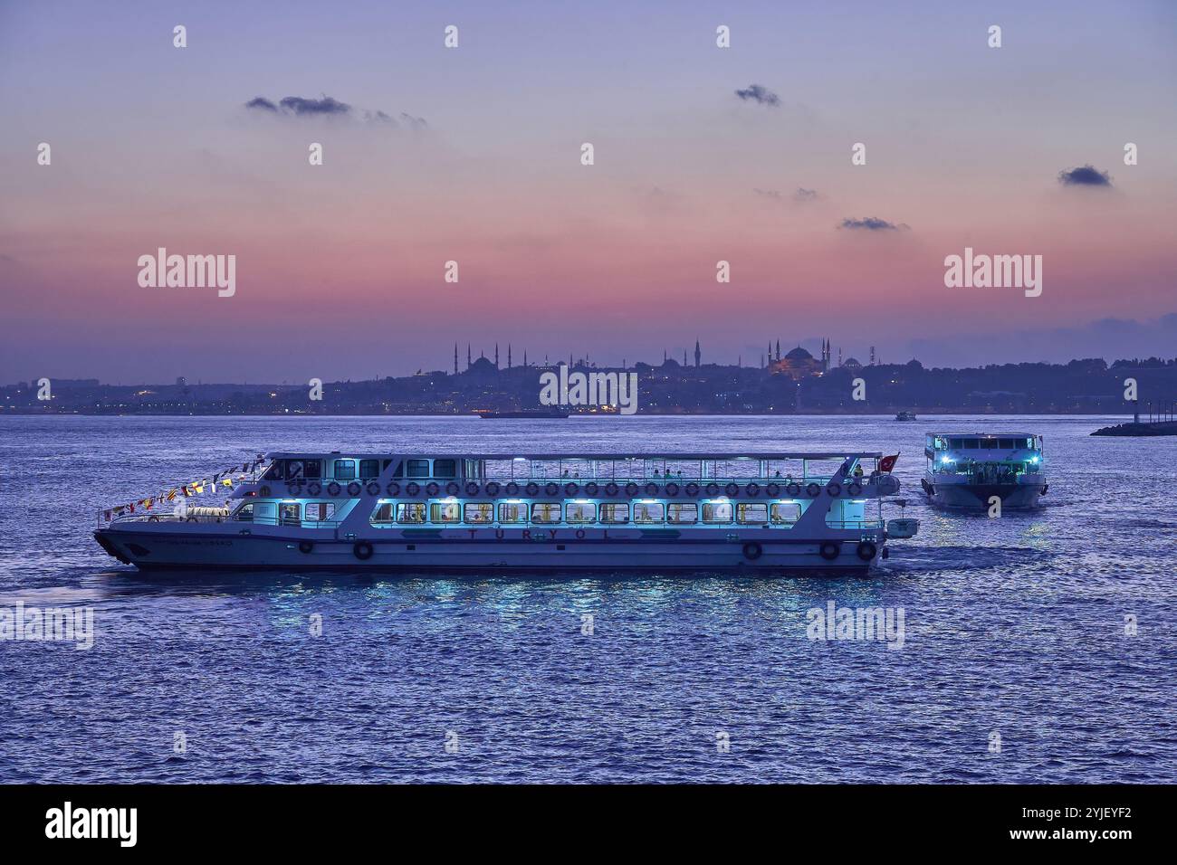 A passenger ferry boat on the Bosphorus in Istanbul at dusk with a pink ...