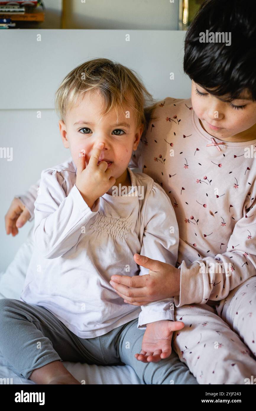 baby touching the nose with the hand and elder child sitting nearby on ...