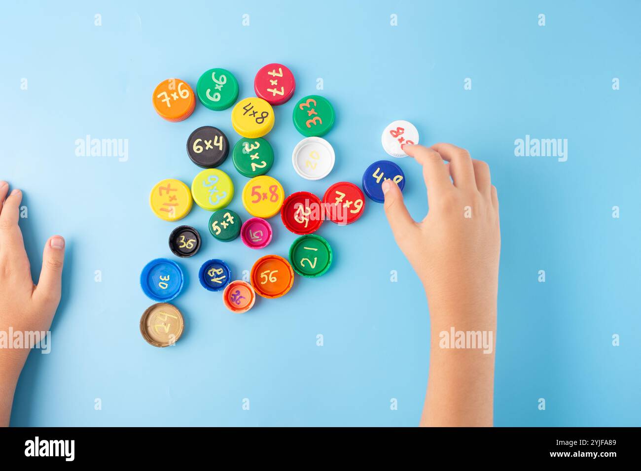 Child hands arranging colorful bottle caps with multiplication problems ...