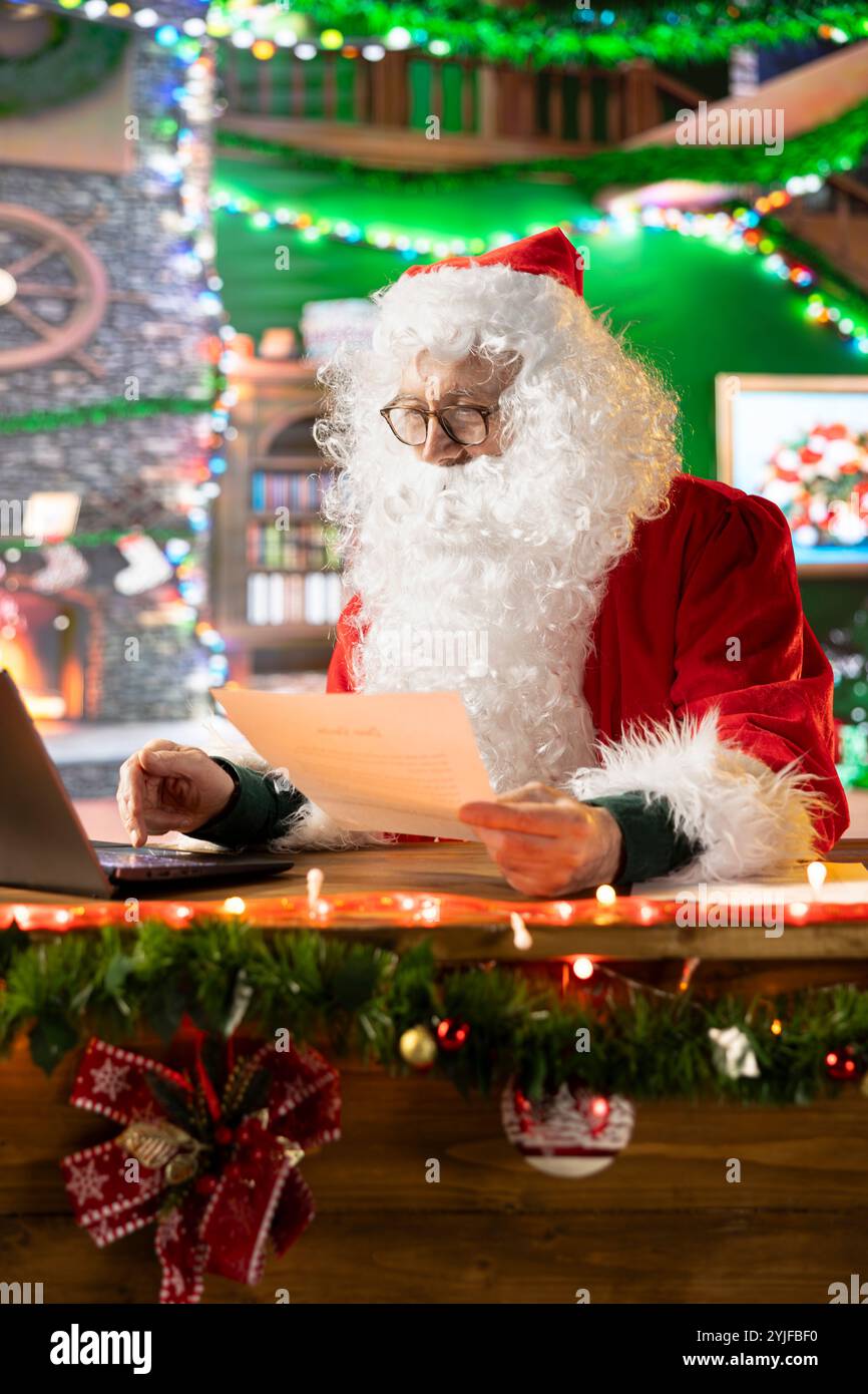 Santa Claus reads a Christmas letter by the fireplace in his workshop ...