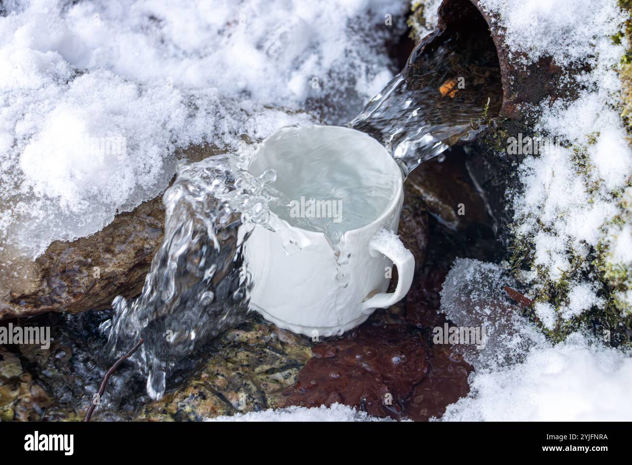 Drinking water flows from a pipe into a cup in a snowy nature, close up ...
