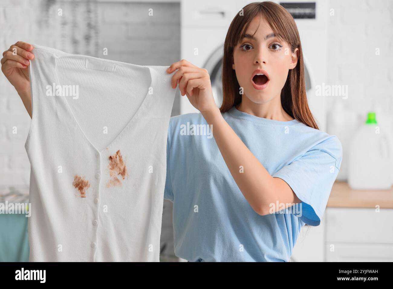 Shocked young woman with stained clothes in laundry room Stock Photo ...
