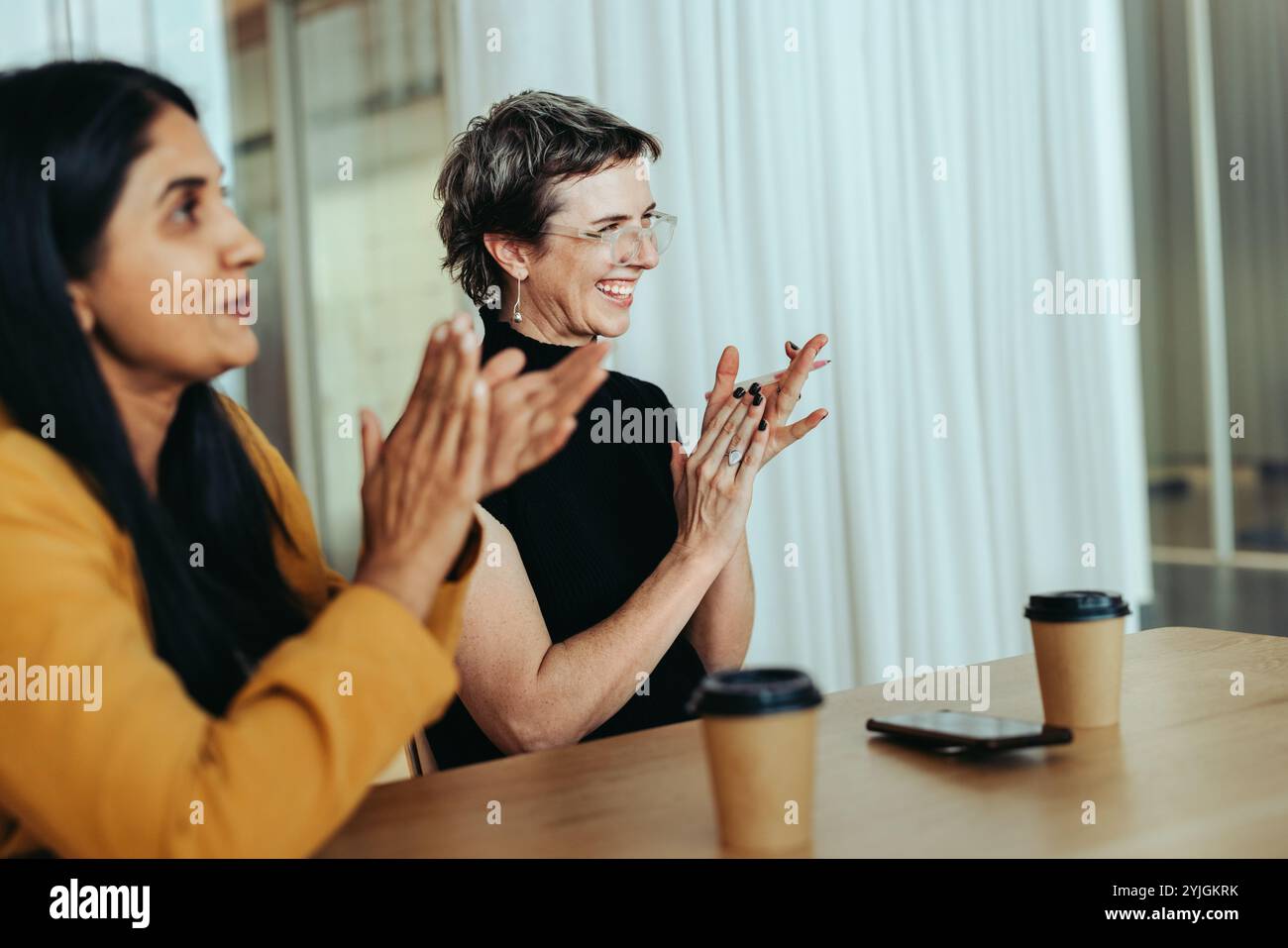 A cheerful office meeting with two people clapping and smiling ...