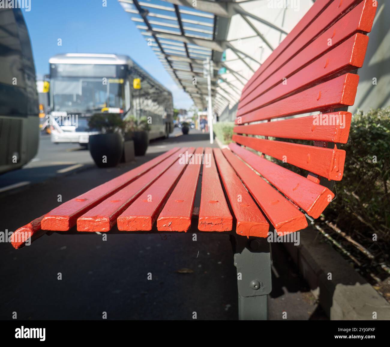 Empty red bench at the bus stop. Out-of-focus buses along the road ...