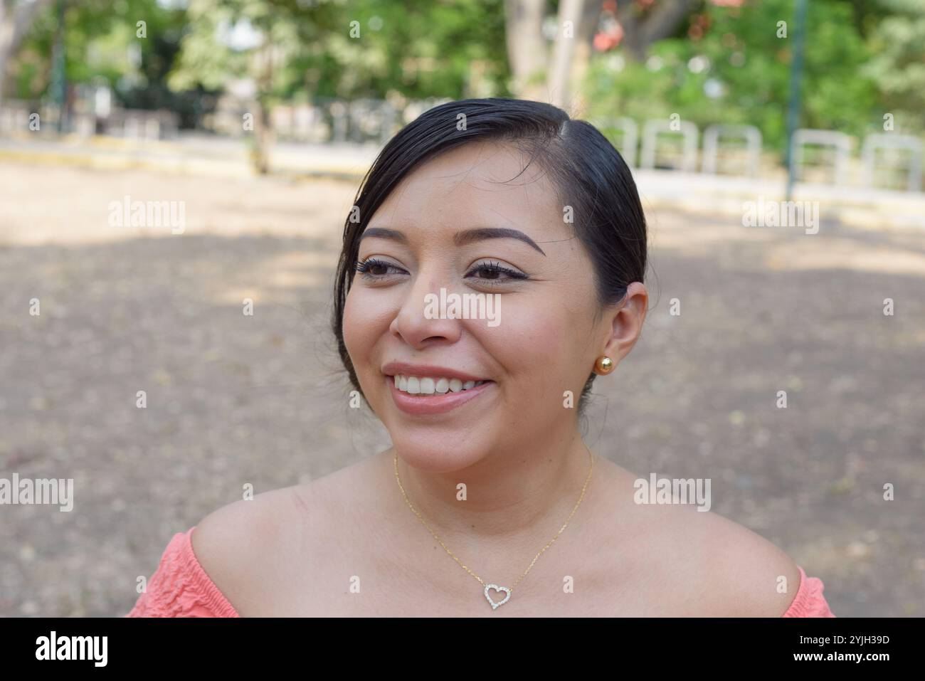A young woman with her hair pulled back in a bun smiles brightly ...