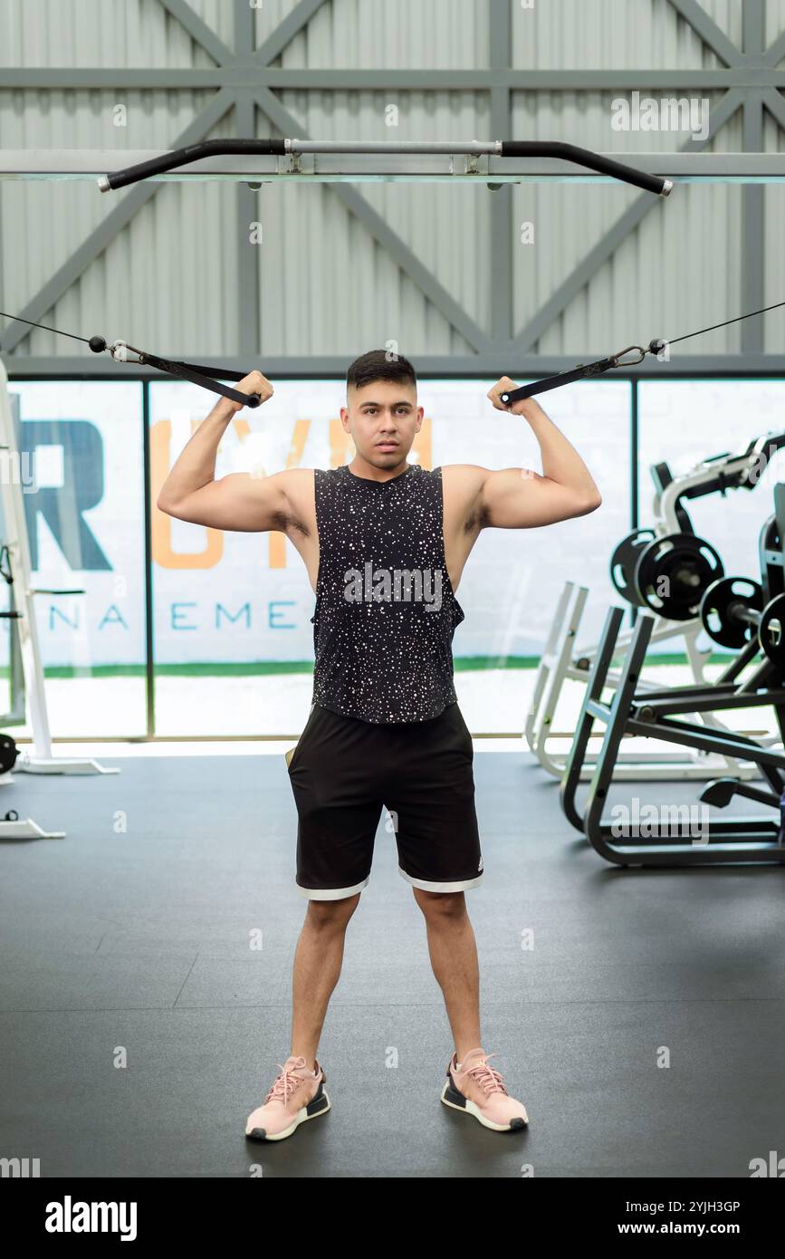 A young man using a cable machine in a gym. He has his arms raised and ...