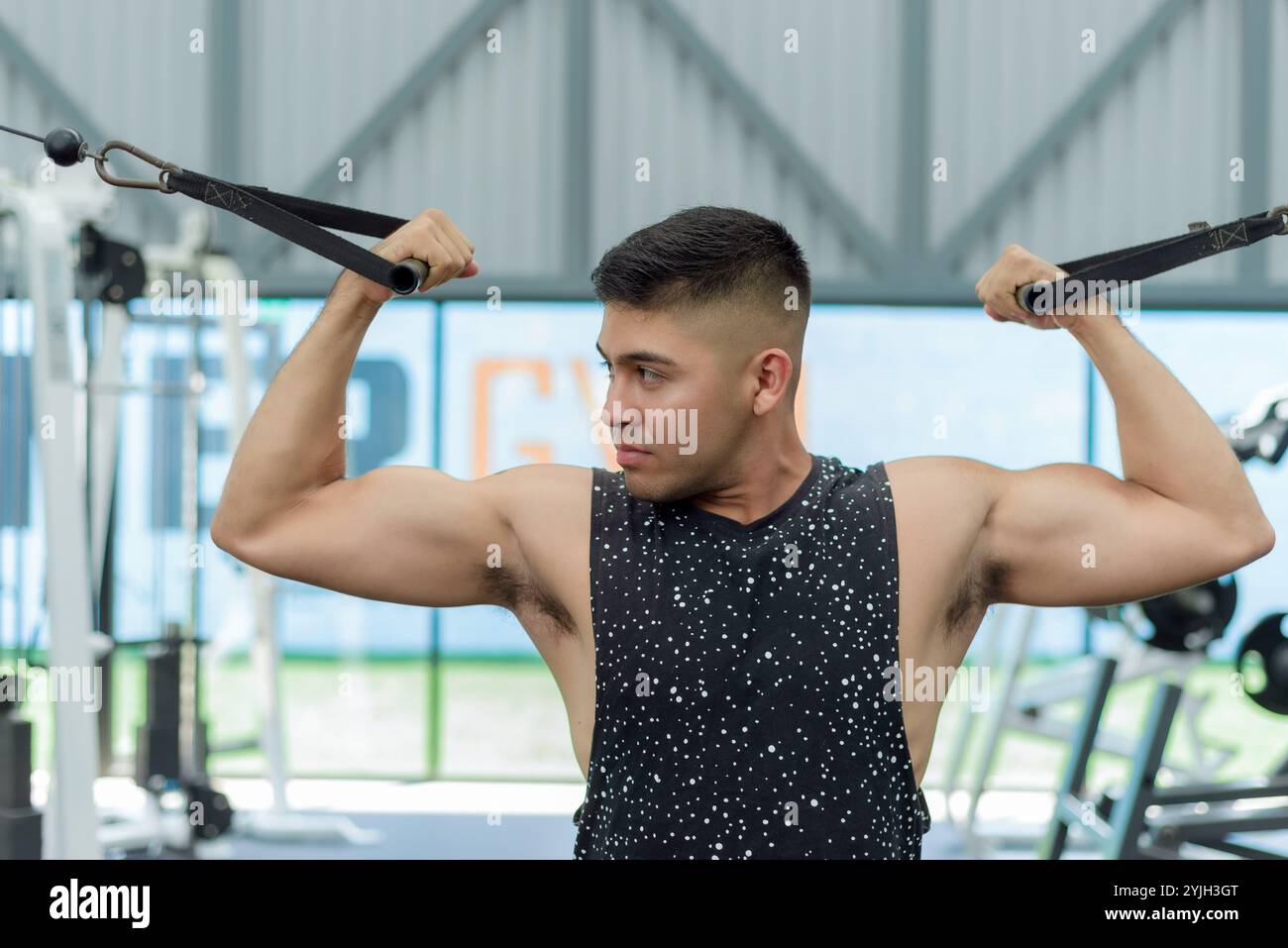A young man using a cable machine in a gym. He has his arms raised and ...