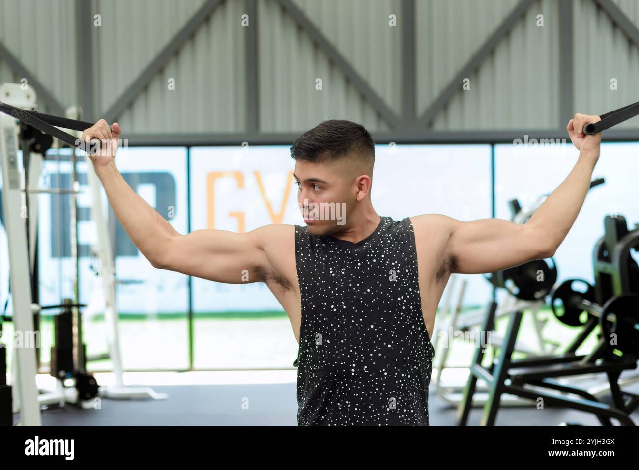 A young man using a cable machine in a gym. He has his arms raised and ...