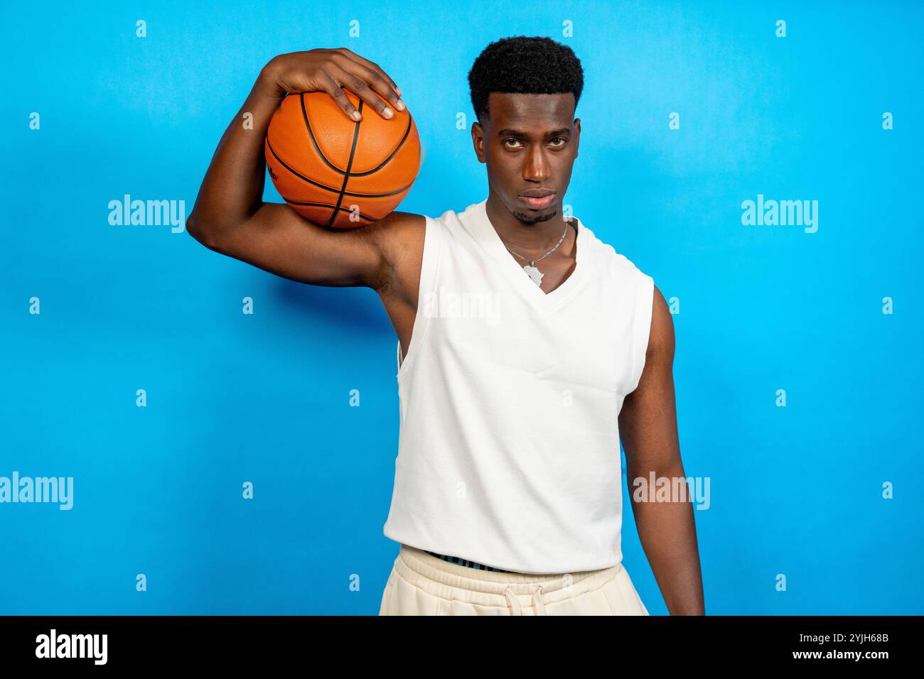 Confident young sportsman holding basketball on shoulder, looking at ...