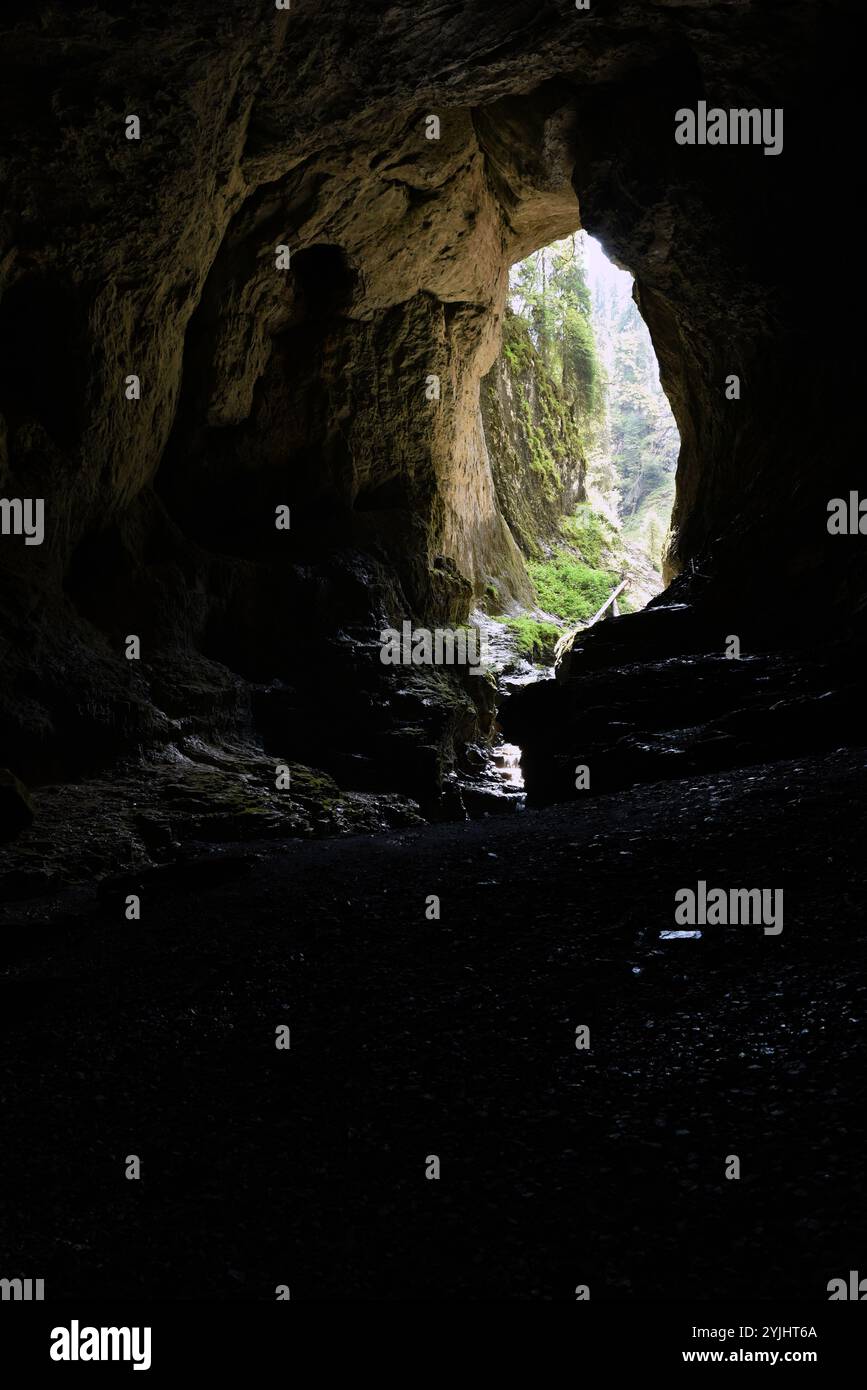 Silhouette of a big cave entrance from inside, water stream flowing ...