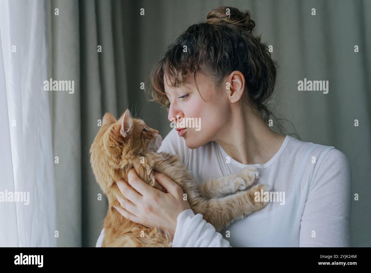 Young woman cuddling her adorable ginger cat, expressing love and affection through a tender ...