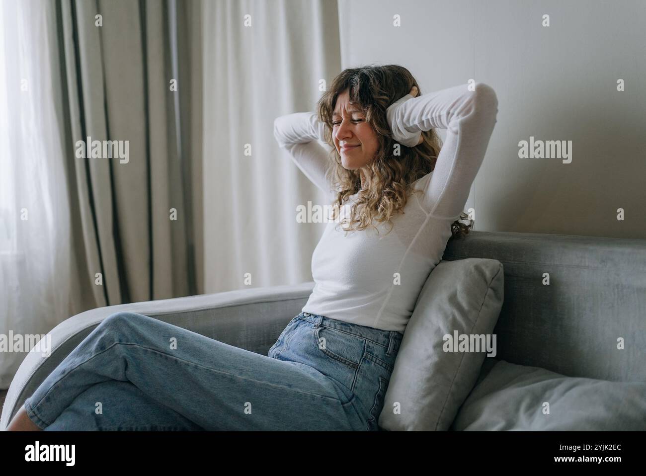 Stressed woman on sofa covering ears from loud noise, feeling annoyed ...