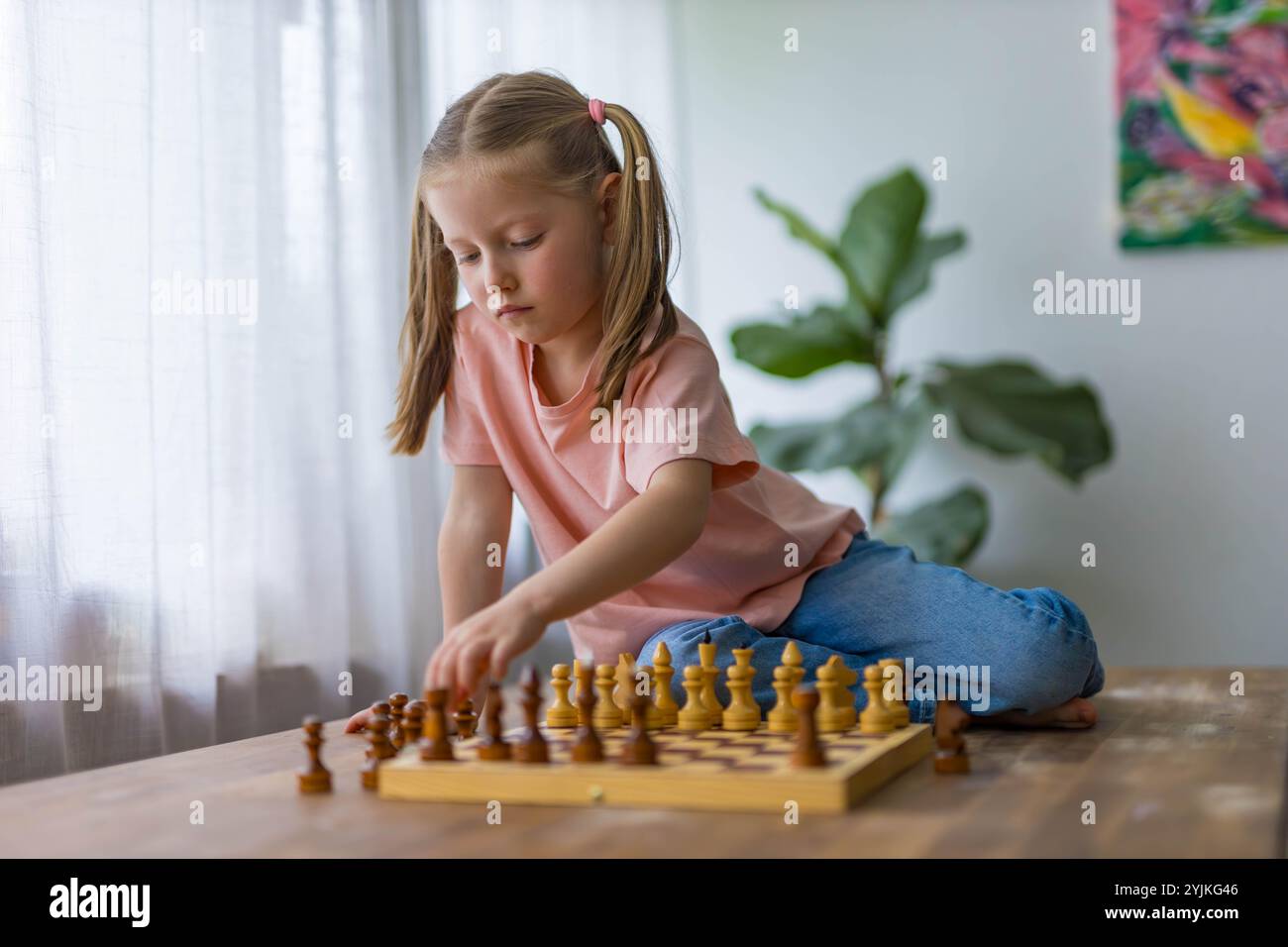 5-year-old girl plays with a mini chess set, focusing intently as she ...