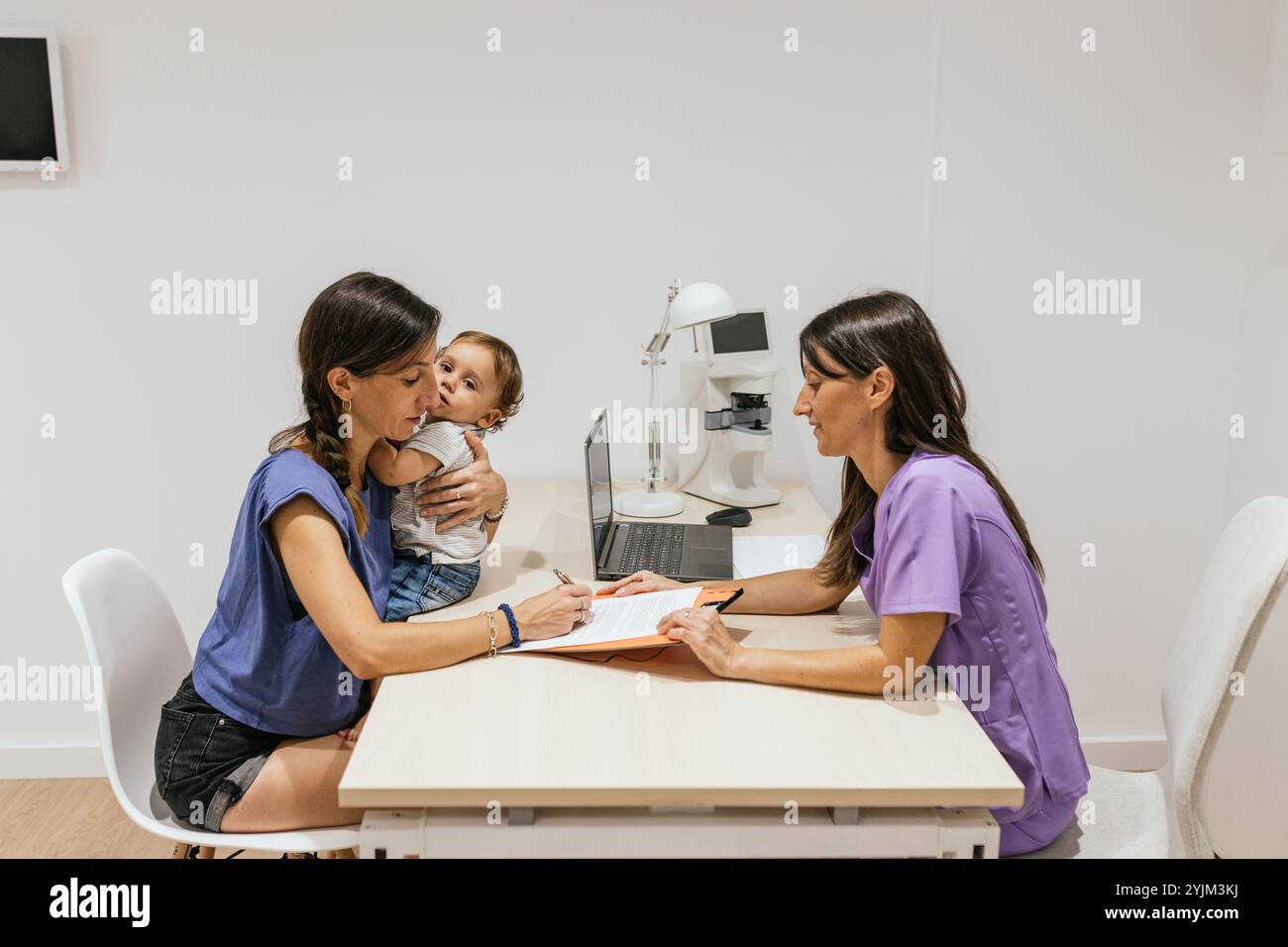 Mother signing medical form for baby at the optometrist's office Stock ...