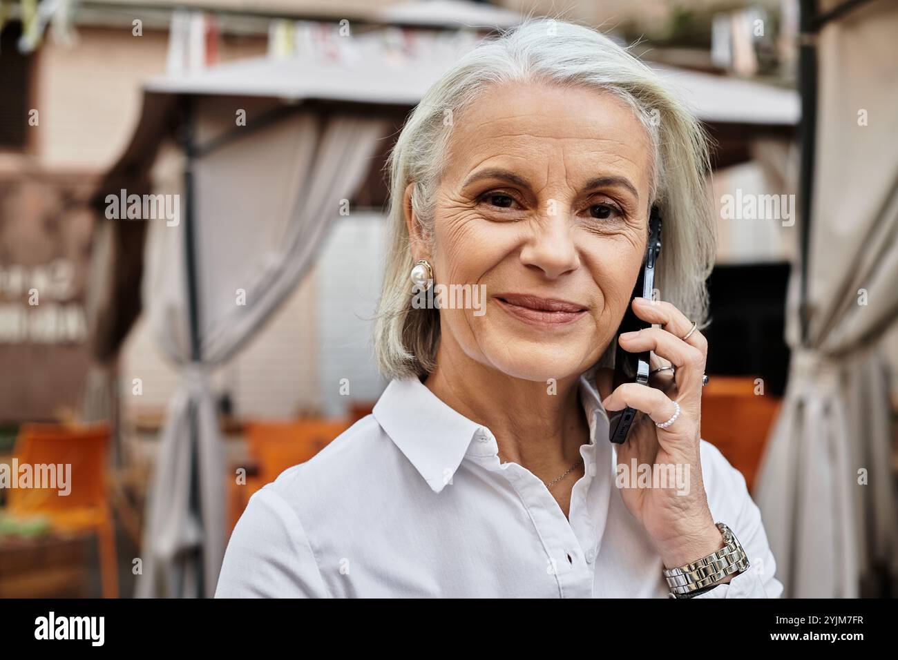 A graceful woman with gray hair smiles as she talks on her phone in a ...