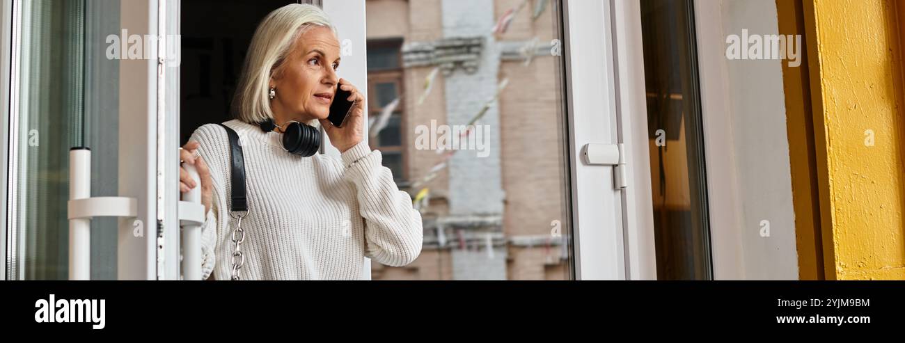 A stylish older woman is talking on her phone while stepping through an ...