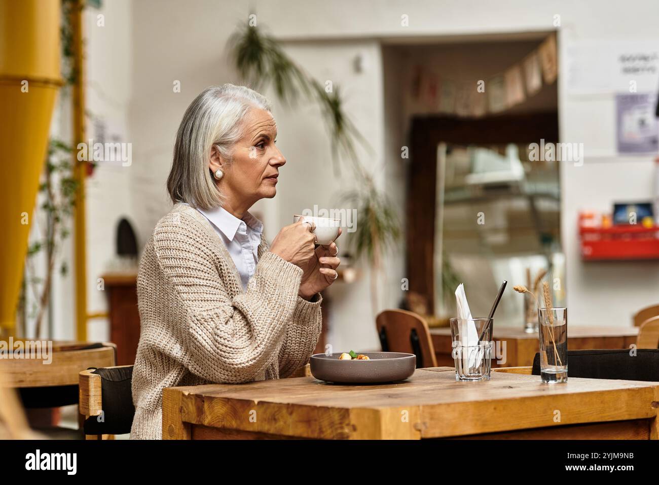 The beautiful mature woman with gray hair sips tea while enjoying a ...