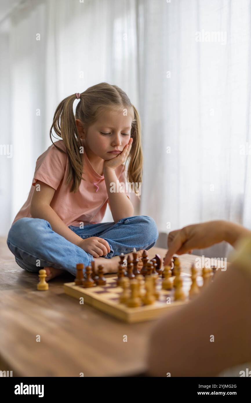 5-year-old girl plays with a mini chess set, focusing intently as she ...