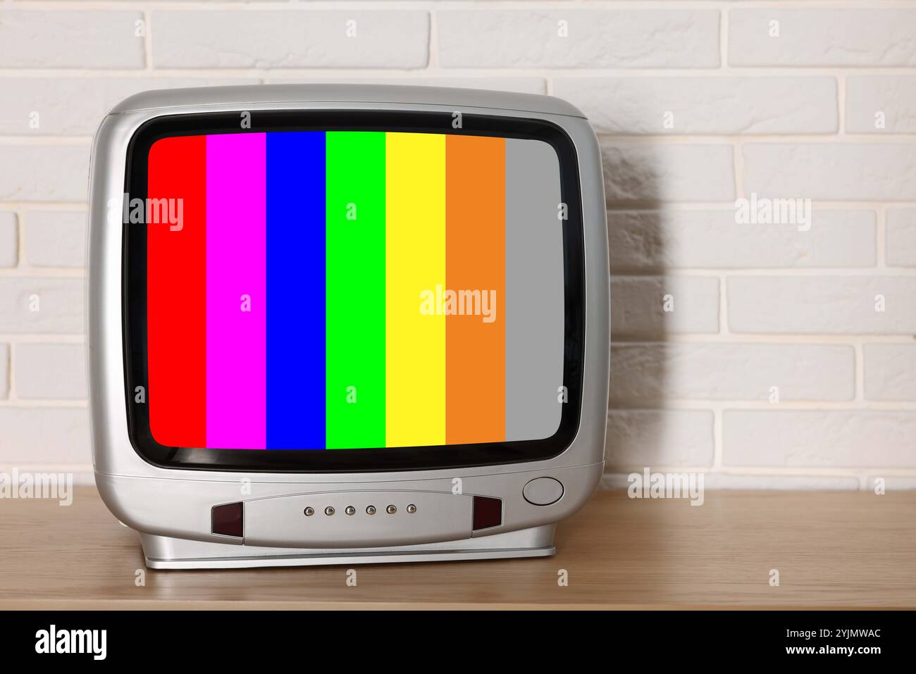 Retro TV set with test pattern on wooden table near white brick wall ...