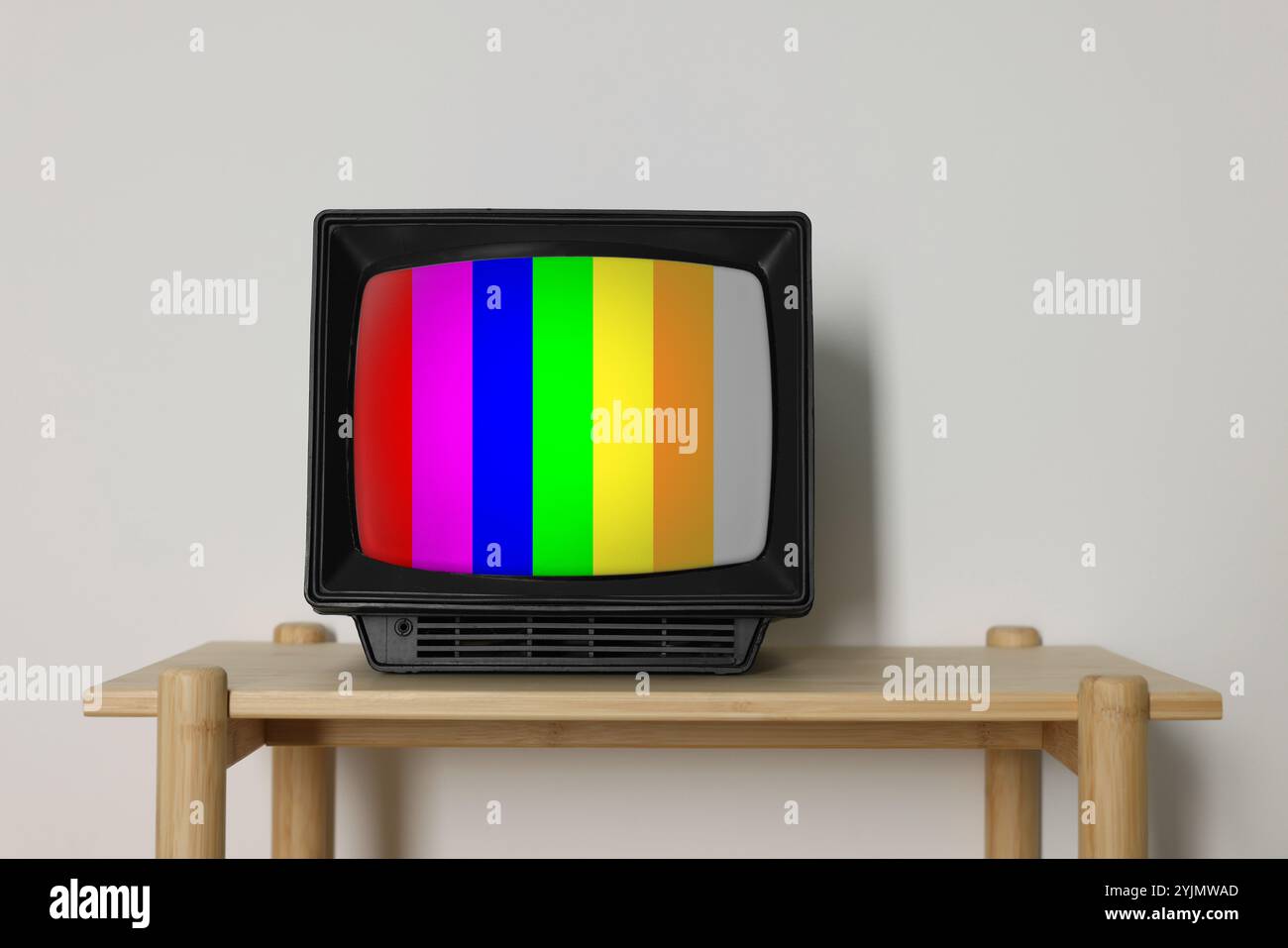 Retro TV set with test pattern on wooden table near white wall. Color ...